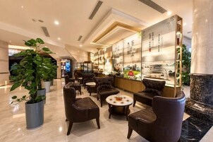 Um saguão de hotel com áreas de estar, balcão de recepção e uma grande planta.