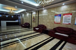 Um saguão de hotel com piso de mármore, sofás vermelhos, um balcão de recepção e um lustre.