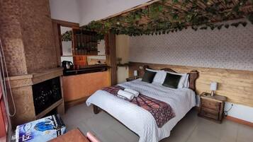Quarto com cama, cabeceira de madeira, mesa de cabeceira e pequena escrivaninha com cadeira.