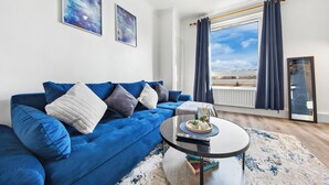 Uma sala de estar moderna com um sofá azul, uma mesa de centro redonda e vista para a cidade através de grandes janelas.