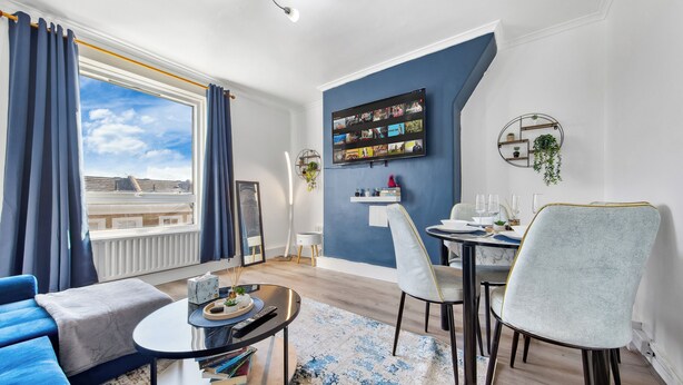 Uma sala de estar moderna com um sofá azul, uma mesa de centro redonda e uma área de refeições com mesa e cadeiras.