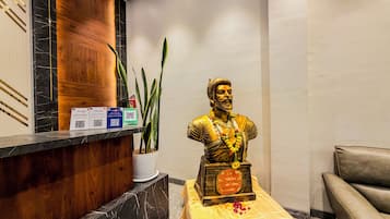 A reception area with a marble counter, a wooden panel, a potted plant, a statue, and a leather couch.