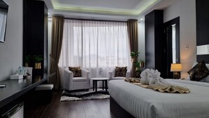 Quarto de hotel moderno com uma cama grande, duas poltronas, uma mesinha e uma escrivaninha com abajur.