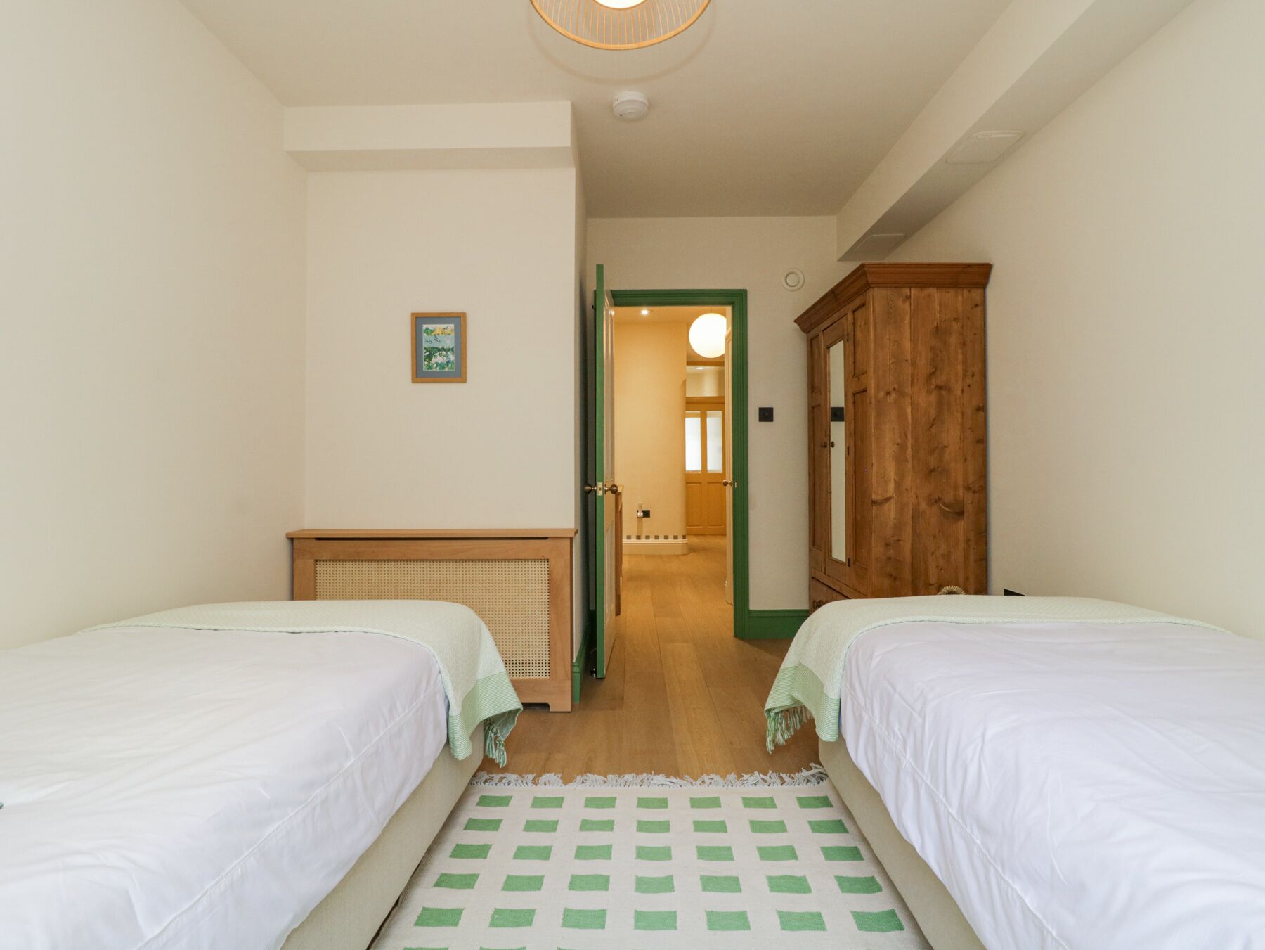 Quarto com duas camas de solteiro, um guarda-roupa de madeira, um pequeno quadro na parede e um corredor que dá para um banheiro.