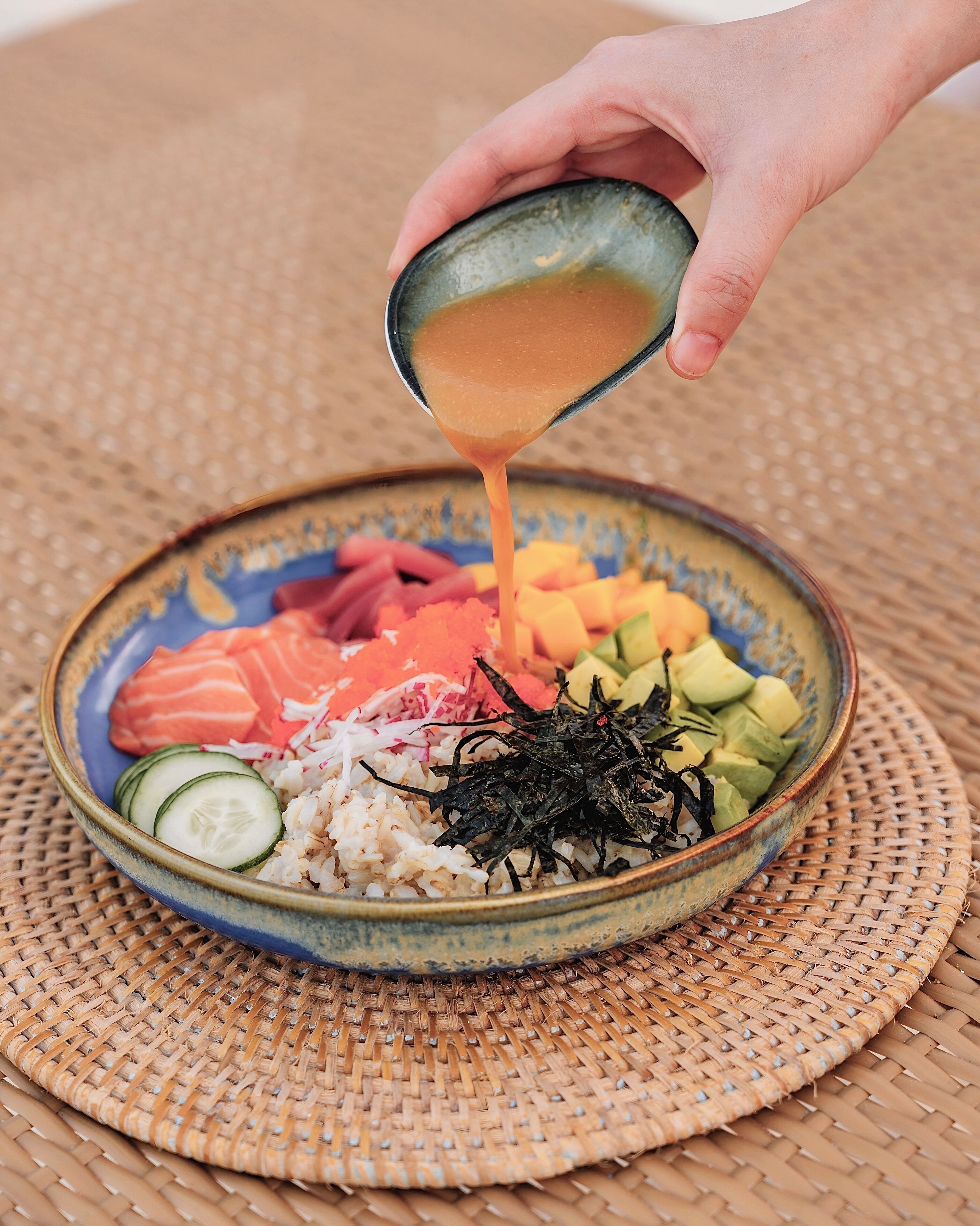 Uma tigela de sashimi com diversos acompanhamentos e uma mão despejando molho sobre ele.