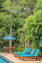 Uma área à beira da piscina com espreguiçadeiras, mesa e guarda-sol.