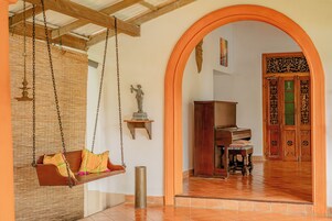 Quarto com balanço de madeira, pequena estante com objetos decorativos, armário de madeira e porta com detalhes elaborados.