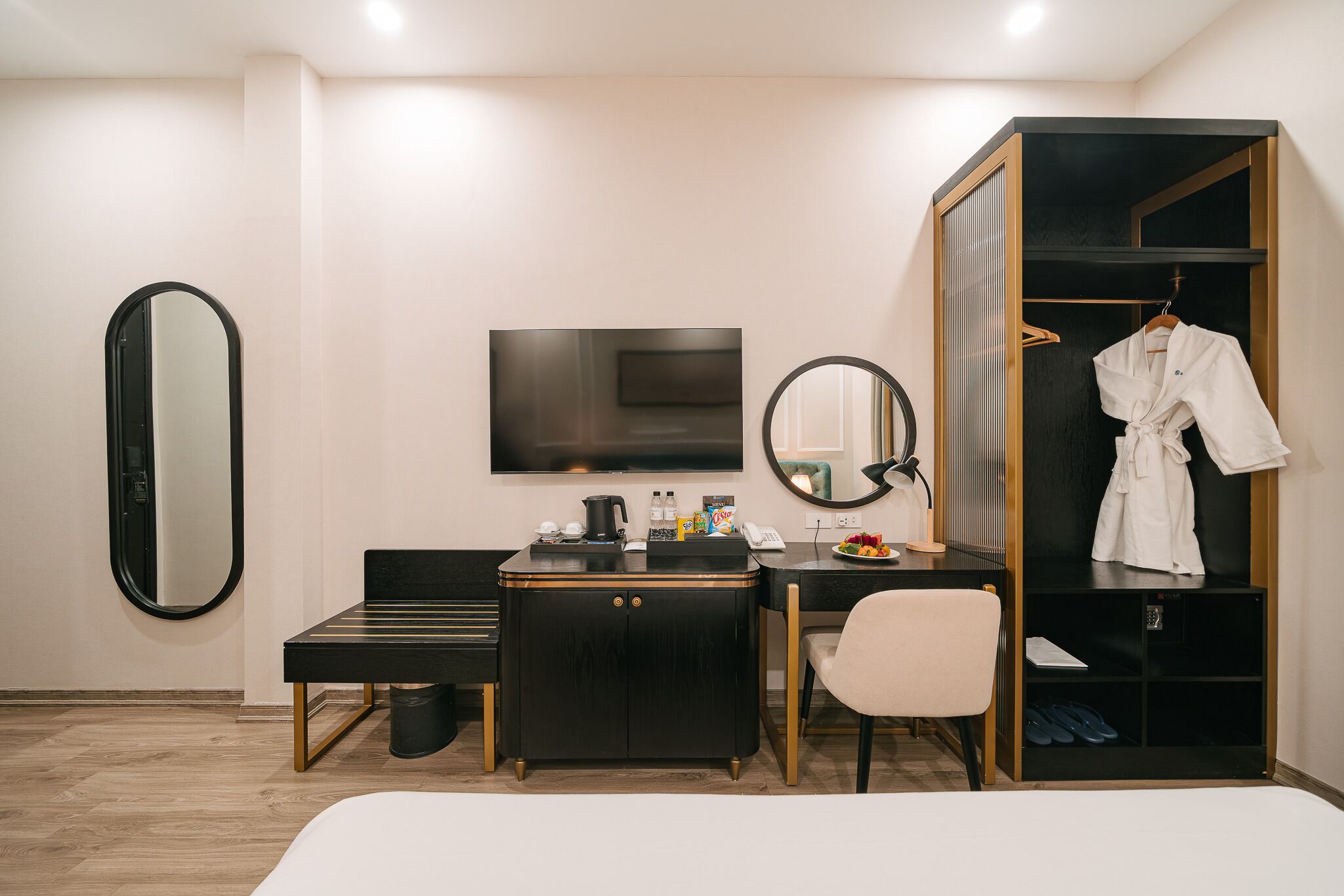 Quarto de hotel moderno com cama, escrivaninha, televisão de tela plana, guarda-roupa, espelho e um pequeno espaço de estar.