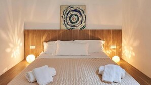 Uma cama bem arrumada com cobertura acolchoada, dois travesseiros e duas toalhas enroladas sobre a cama.