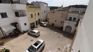 Um pátio com dois carros estacionados, um edifício com varanda e uma parede branca com uma janela.