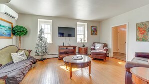 Uma sala de estar ampla com assoalho de madeira, uma televisão de tela grande e um pinheiro de Natal.