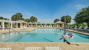 Piscina com espreguiçadeiras e guarda-sóis, cercada por árvores e áreas cobertas.
