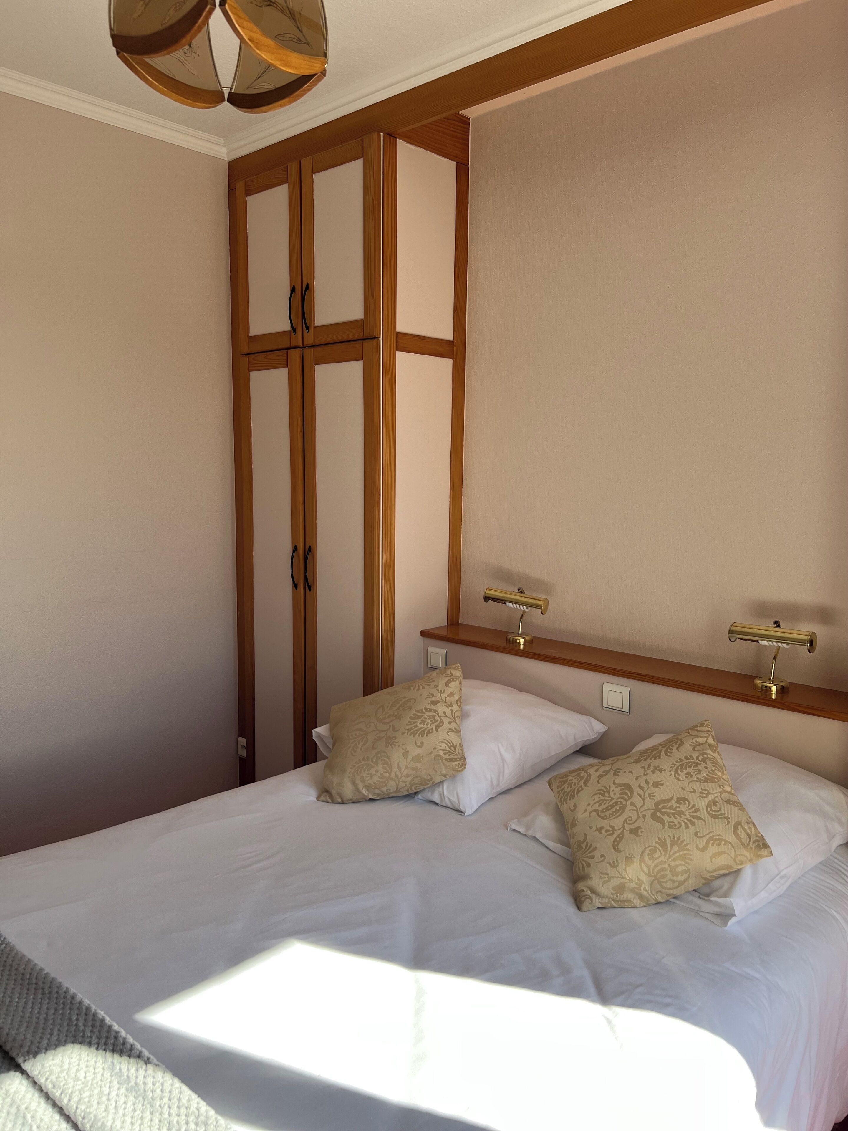 Quarto com uma cama, duas mesas de cabeceira, um guarda-roupa de madeira e um ventilador de teto.