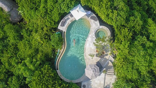 Vista aérea de uma piscina privativa rodeada por vegetação exuberante, com uma pessoa nadando.