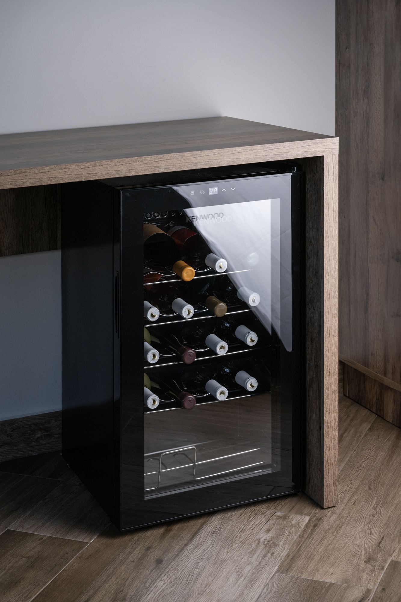 Um frigorífico para vinhos com espaço para garrafas embutido, posicionado sob uma mesa de madeira.