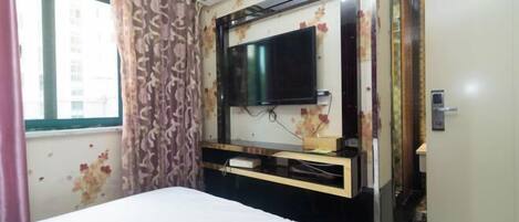 Quarto de hotel com cama, televisão na parede, aparelho de ar condicionado e uma porta.