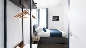 Quarto de hotel moderno com cama, mesa de cabeceira e guarda-roupa com um cabide de madeira.