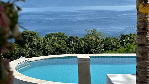 Piscina com vista clara para uma montanha e o oceano ao fundo.