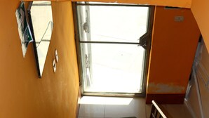 Uma escadaria com degraus alternados em vermelho e bege, um corrimão de metal e vista para o exterior através de uma porta de vidro.