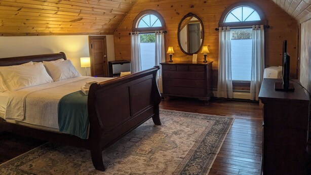 Quarto com teto de madeira, uma cama, cômoda, espelho e televisão.