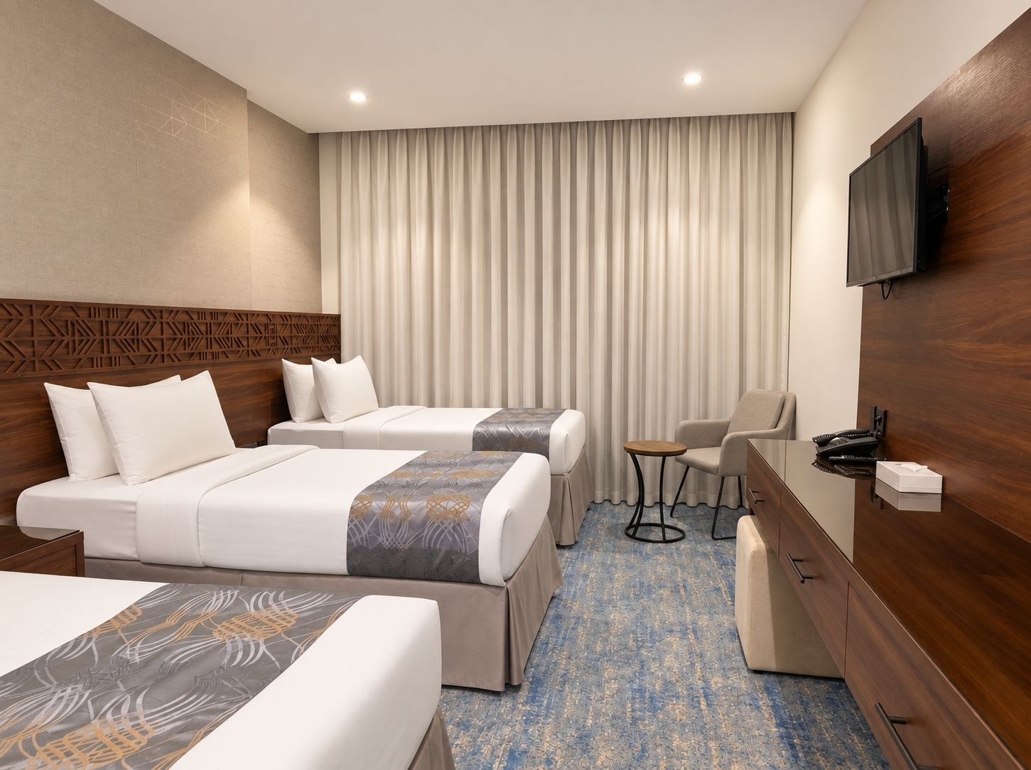 Quarto de hotel com duas camas, uma escrivaninha, uma cadeira, uma televisão e uma janela grande com cortinas.