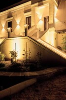 Um edifício com escadaria que leva a uma varanda, rodeado por um jardim com plantas e flores.