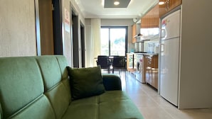 Uma sala de estar moderna com um sofá verde, uma cozinha com armários de madeira e uma área de jantar com cadeiras.
