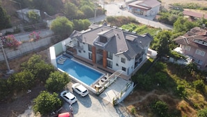 Uma casa grande com piscina, vários carros e um jardim bem cuidado.
