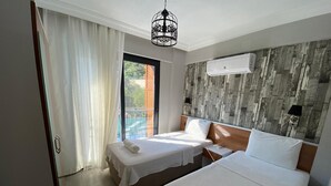Quarto de hotel com duas camas, uma janela grande com cortinas, um candeeiro no teto e um ar condicionado fixado na parede.