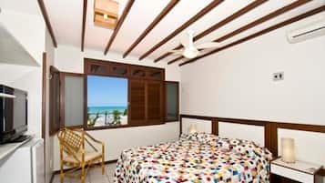 Quarto com cama, poltrona, televisão e janela com vista.