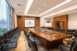 Sala de conferência com uma mesa comprida, cadeiras pretas e uma tela de projeção.