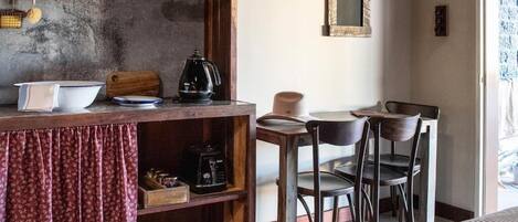 Uma cozinha acolhedora com bancada de madeira, chaleira e cafeteira. Há uma mesa com cadeiras e uma janela com vista.