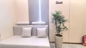 Quarto moderno com sofá-cama, uma planta em vaso e luminária vertical.