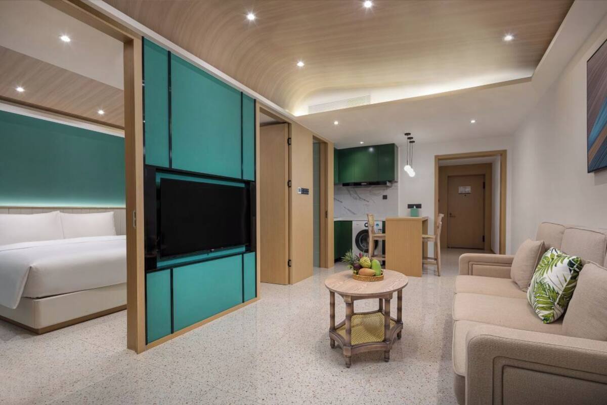 Quarto de hotel moderno com uma cama, televisão, pequeno espaço de refeições e cozinha compacta.