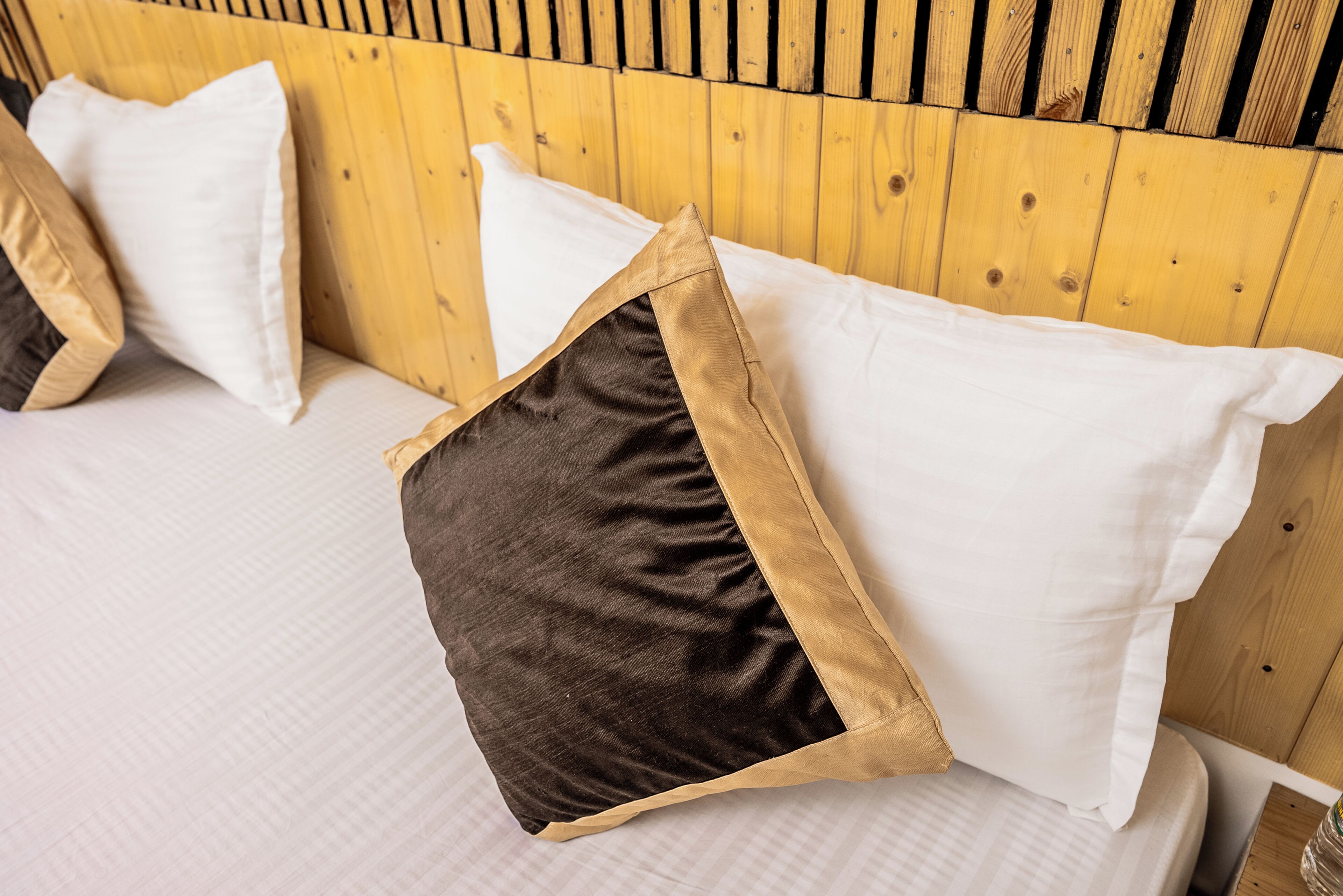 Cama com roupa de cama branca e duas almofadas, uma com detalhes dourados.