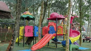 Um parquinho com diversas estruturas de lazer, incluindo escorregadores e áreas de escalada, cercado por árvores.