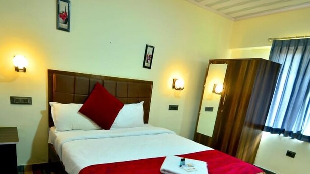 Quarto de hotel com uma cama, um cobertor vermelho e uma mesinha de cabeceira.