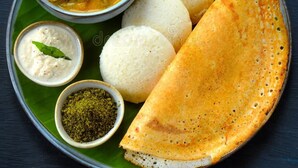 Um prato com um dosa, três bolas de idli, uma tigela de sambar, uma tigela de chutney de coco e uma pequena tigela de chutney verde.