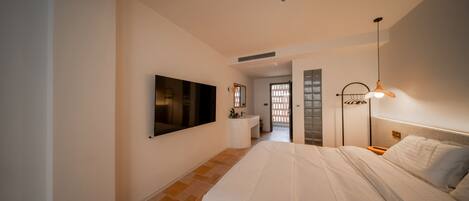 Quarto com cama, televisão na parede, mesa de cabeceira e abajur.