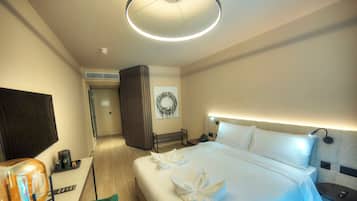 Quarto de hotel com uma cama grande, uma escrivaninha, uma cadeira, uma TV e luminária na parede.