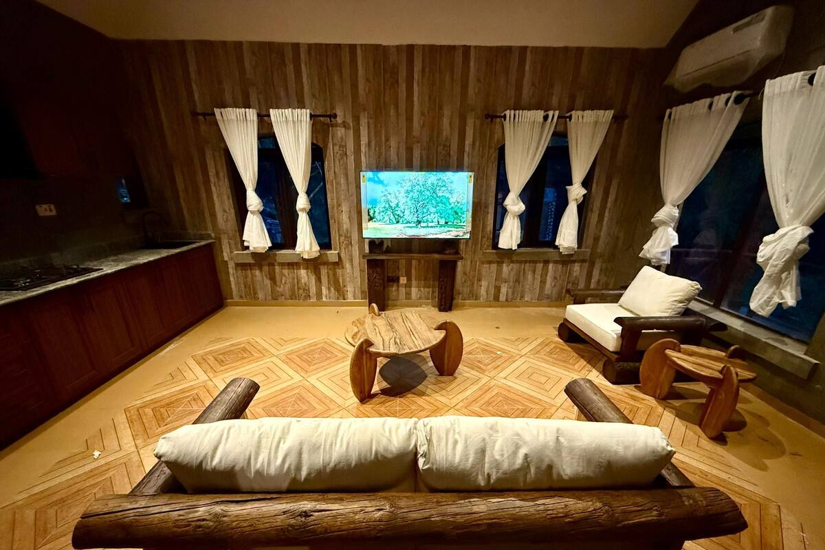 Um quarto aconchegante com piso de madeira, um sofá, uma TV e cortinas.