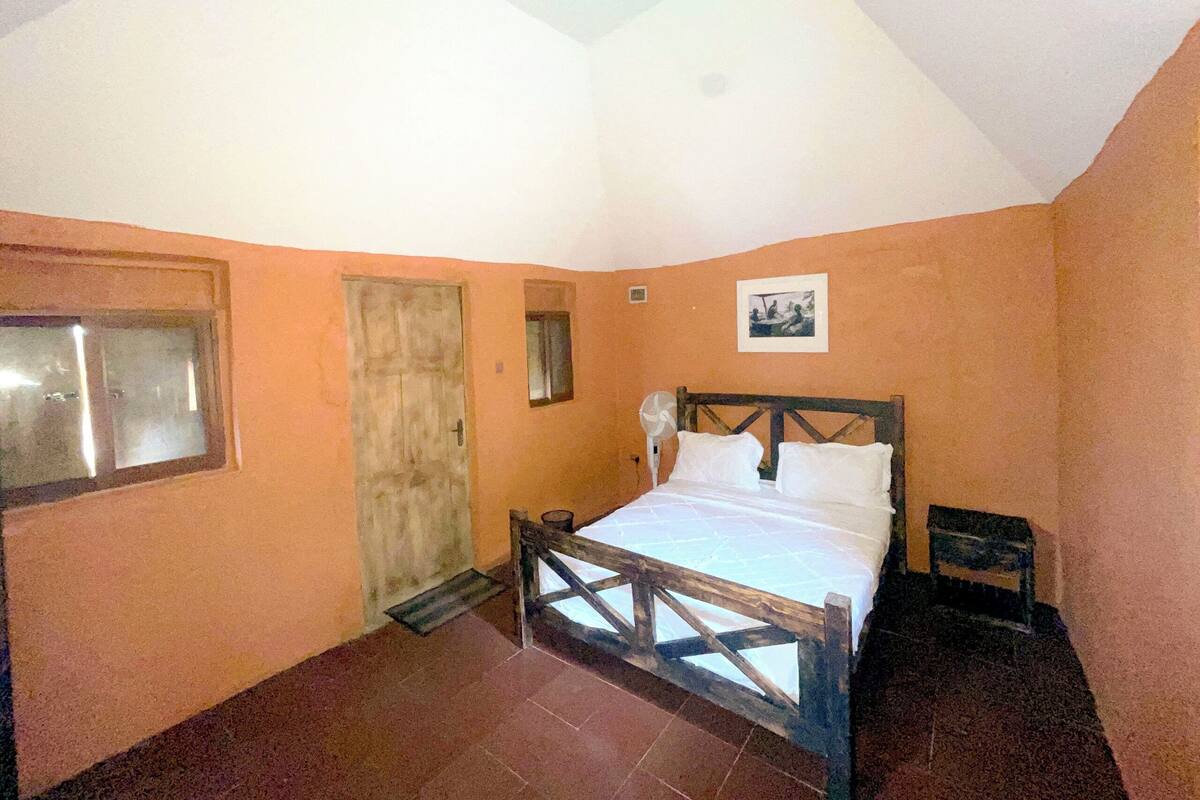 Quarto com cama de madeira, mesa de cabeceira pequena, janela e porta.