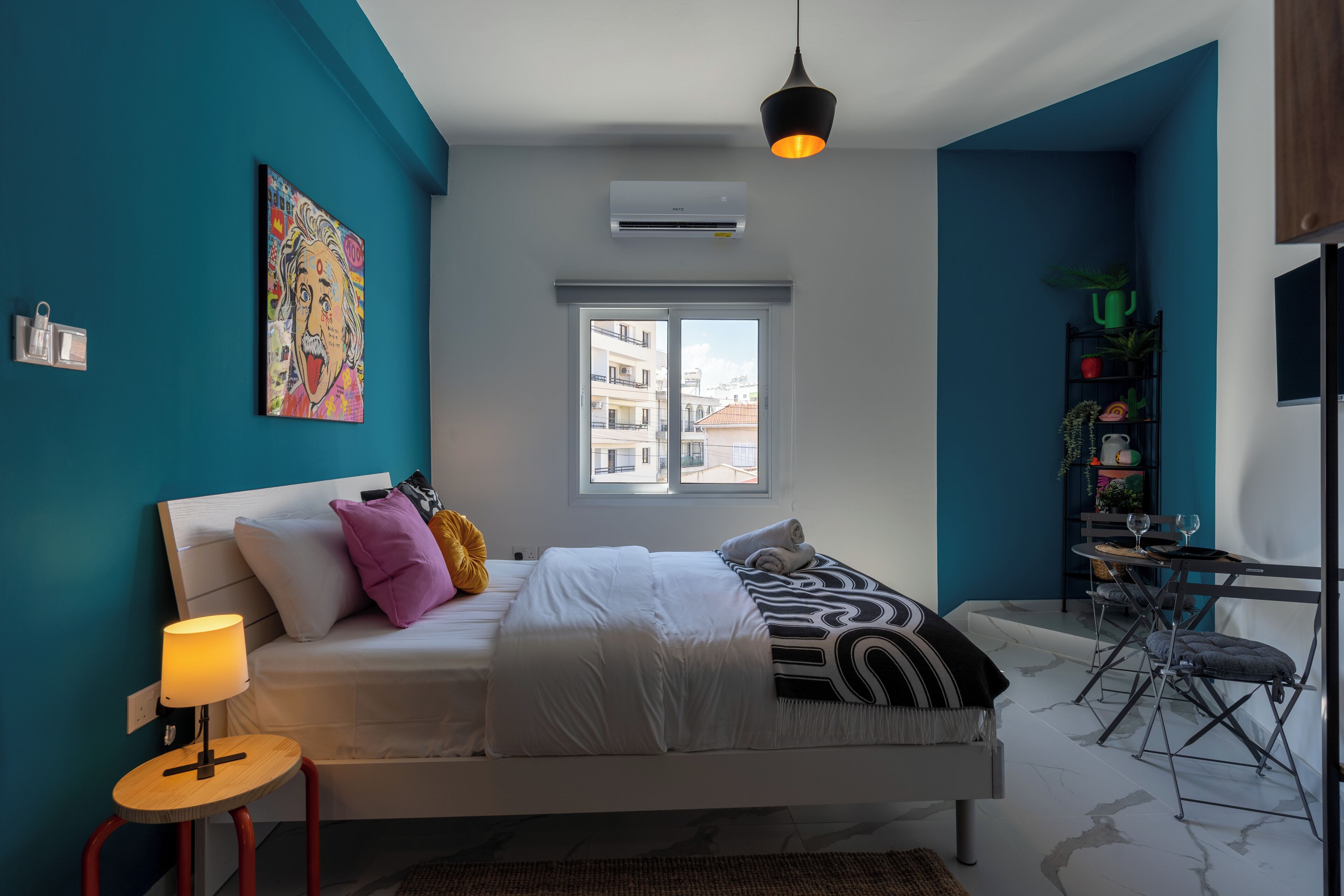 Quarto moderno com cama, abajur e janela com vista para edifícios.