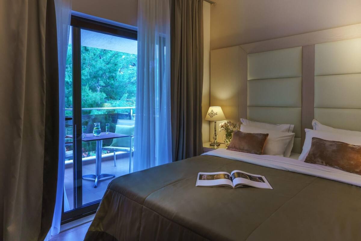 Quarto de hotel com uma cama, mesa de cabeceira com abajur, janela com cortinas e vista para o exterior.