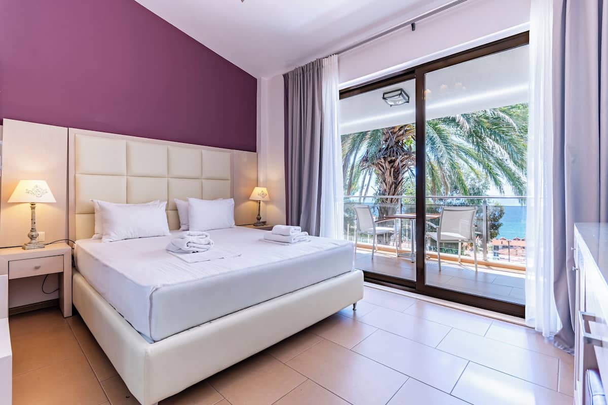Quarto de hotel com uma cama grande, duas luminárias de cabeceira, mesa de cabeceira e varanda com vista para o mar.