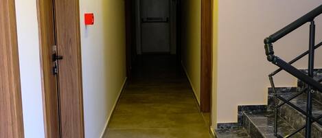 Corredor de hotel com portas de madeira, uma placa indicando números de quarto e uma escadaria com acabamento em mármore.