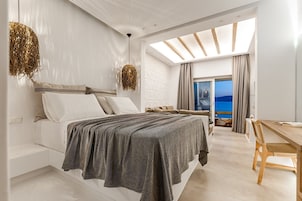 Quarto moderno com uma cama grande, uma escrivaninha de madeira e vista para o mar.