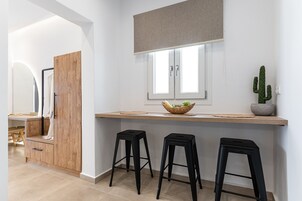 Cozinha moderna com bancada de madeira, dois banquinhos pretos, janela com vista e uma planta de cacto.