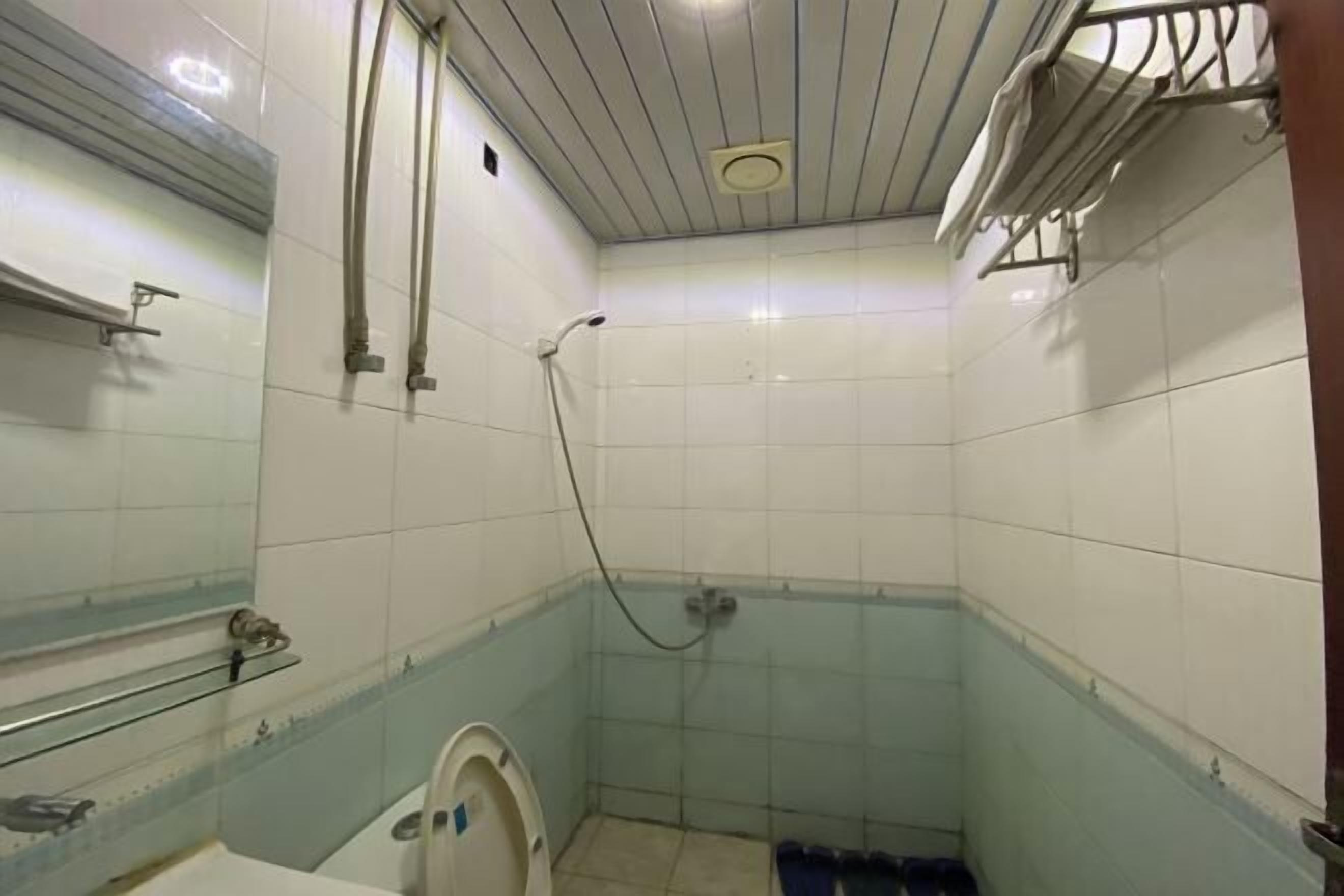 Um banheiro pequeno com azulejos, um chuveiro, um vaso sanitário e uma prateleira de vidro.