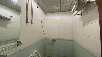 Um banheiro pequeno com azulejos, um chuveiro, um vaso sanitário e uma prateleira de vidro.